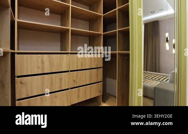 Wooden walk in closet with drawers, empty oak shelves, green curtain ...