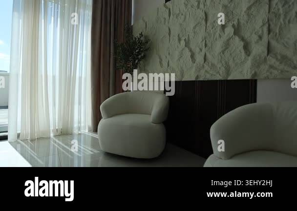 Sunlit minimalist lounge with armchairs. Textured stone wall and sheer ...