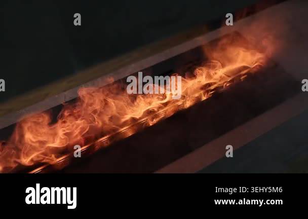 Intense orange flame along black metal, highenergy burner shot at night ...