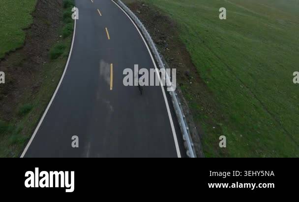 Aerial footage of riding road bike in the beautiful grassland mountain ...