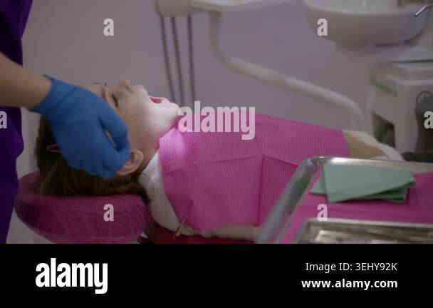 A young child relaxes in a dental chair, wearing a pink bib. The calm ...