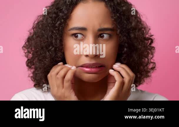 A woman with dark skin and curly hair displays a fearful expression ...