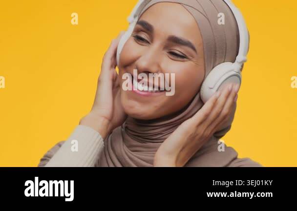 A woman in a headscarf is wearing white headphones and smiling while ...