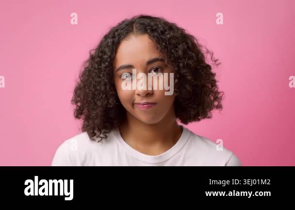 A young woman with curly hair looks towards the camera with a gentle ...