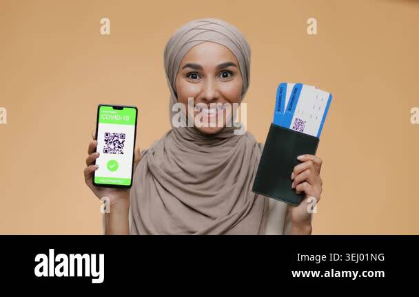 A woman stands against a plain background holding a smartphone ...
