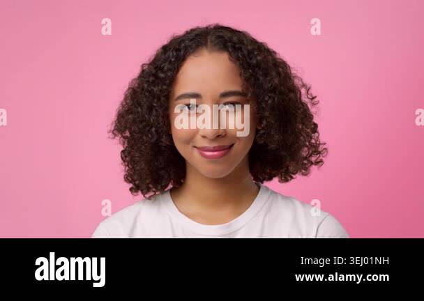 A young woman with curly hair is smiling directly at the camera. She ...