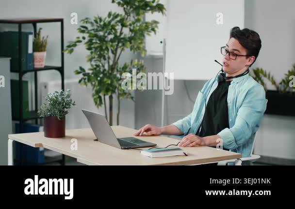 Young man with light skin wears headphones while typing on a laptop in ...