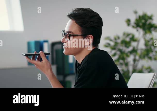 Young man with light skin and glasses is speaking into a smartphone in ...