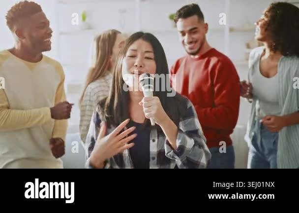 A woman with long dark hair sings into a microphone while friends stand ...