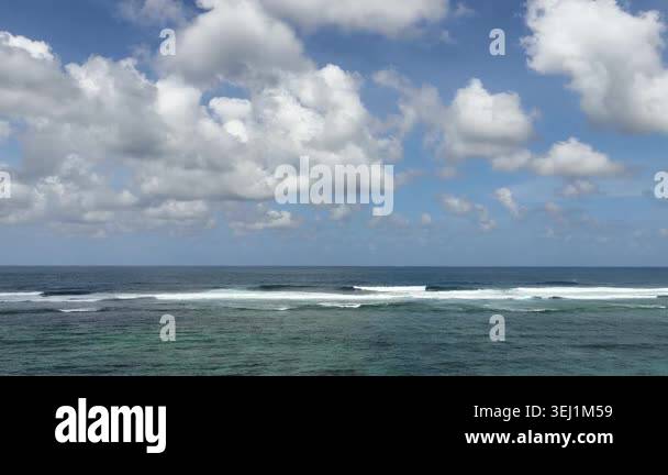 Calm ocean waves rolling over coral reef under a blue sky with fluffy ...
