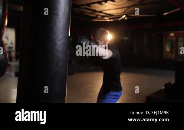 Caucasian kickboxer with gloves training and punching a heavy bag in a ...