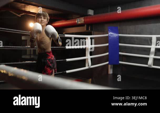 Determined young fighter in boxing gloves training alone in the ring ...
