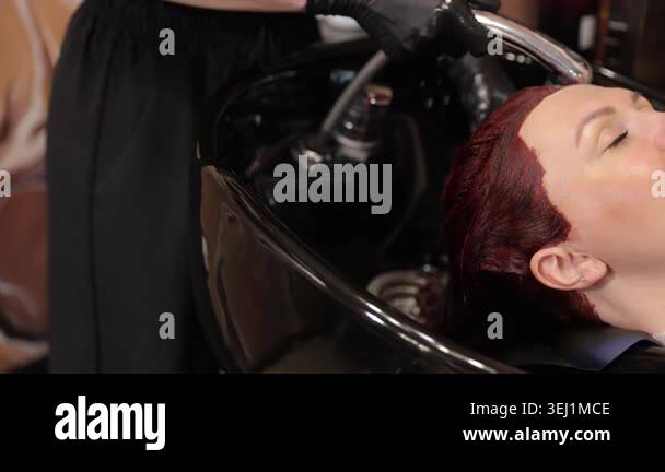 Professional hairstylist in black gloves washing red hair dye from a ...