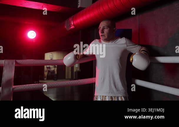Tired male fighter with boxing gloves leaning on the ropes, taking a ...