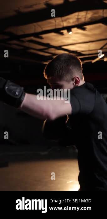 Determined young fighter in black gloves training with a punching bag ...