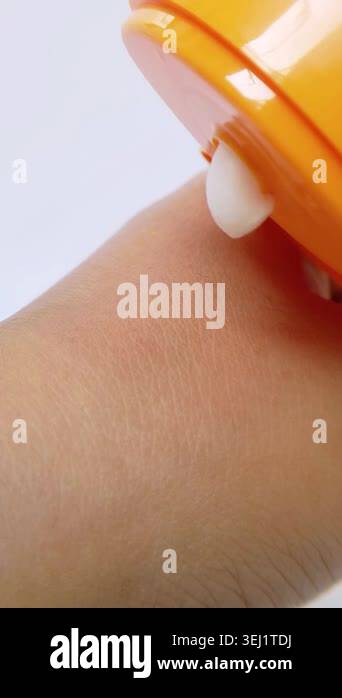 Pouring white cream from orange beauty product onto hand skin. Close up ...