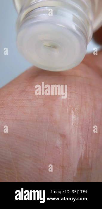 Pouring clear liquid from transparent product packaging onto hand skin ...