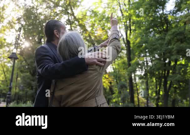 Elderly couple hugging and pointing at the sky while walking in a ...