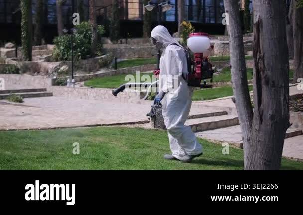 Worker in protective suit spraying garden with pesticide using backpack ...