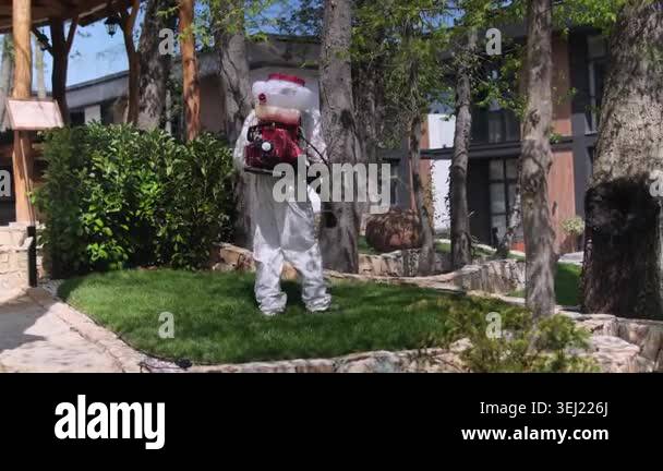 Worker in protective suit spraying garden with pesticide using backpack ...