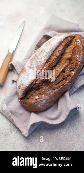Fresh, homemade dark rye bread loaf resting on a linen napkin with a ...