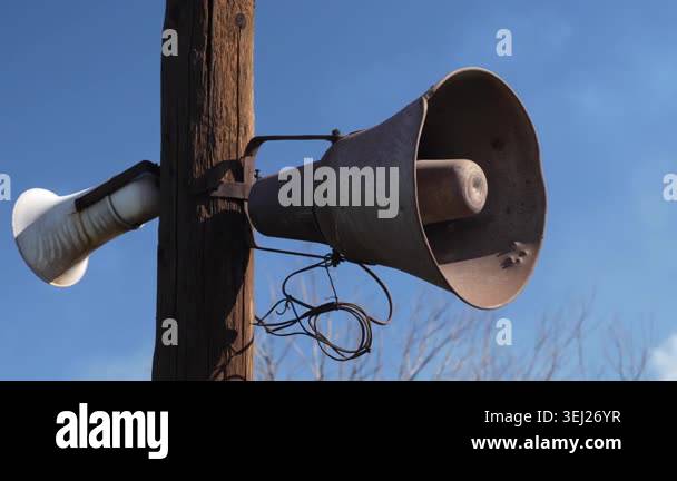 Vintage aluminum loudspeaker mounted on a wooden utility pole against ...