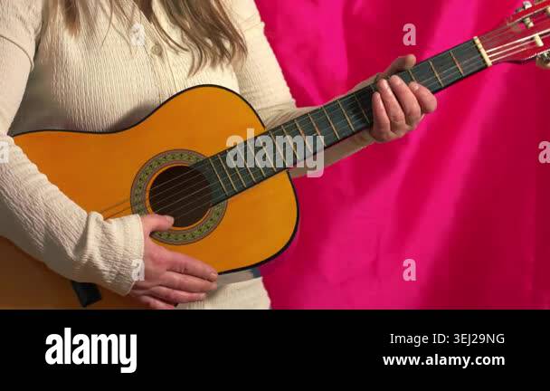 Woman playing acoustic guitar on pink background medium zoom shot slow ...