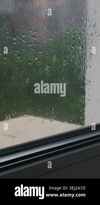 Heavy rain droplets run rapidly down the glass window pane. Blurred ...