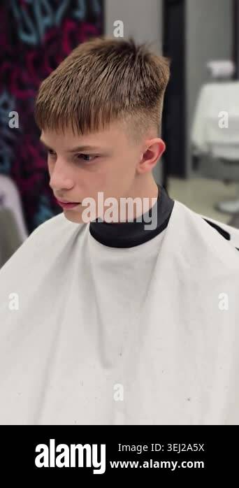 blonde female barber using hair clippers and comb to cut teenage boy ...