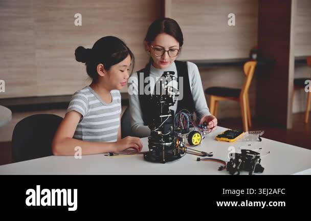 Helpful female teacher guide young schoolgirl to assemble robotic toy ...