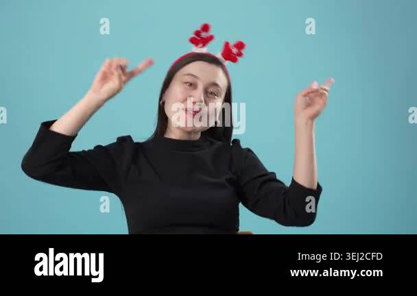 A happy young woman wearing a festive Christmas headband dances ...