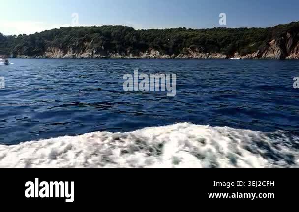 White wake of a fast boat sailing along the rocky coastal cliffs and ...
