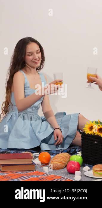 Smiling female sitting on blanket, clinking drinks and tasting juice ...