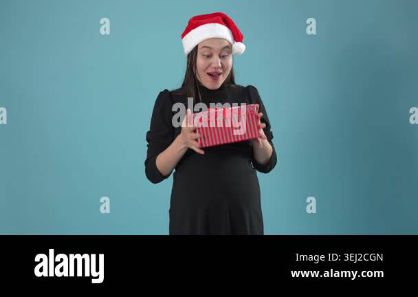 Smiling pregnant woman wearing red santa hat opens festive striped ...
