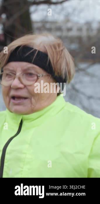 Senior woman in green jacket doing warm up exercises outdoor in the ...