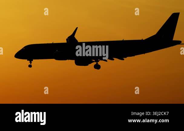 A plane takes off into the sky as the sun sets, creating orange and ...