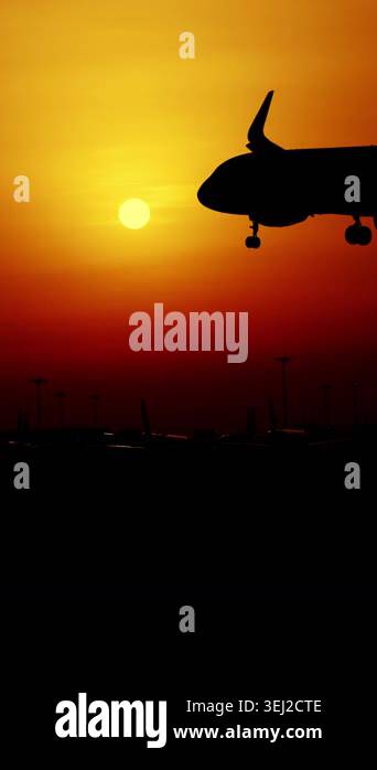 An airplane approaches the runway as the sun sets. The sky fills with ...