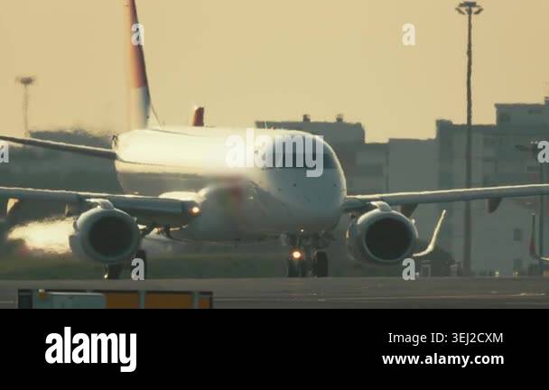 An airplane is taxiing on the runway at an airport as the sun sets in ...