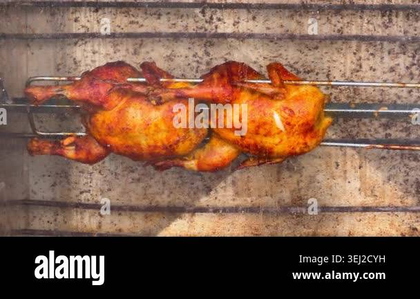 Pair of golden brown roasted whole chicken poultry rotating on metal ...