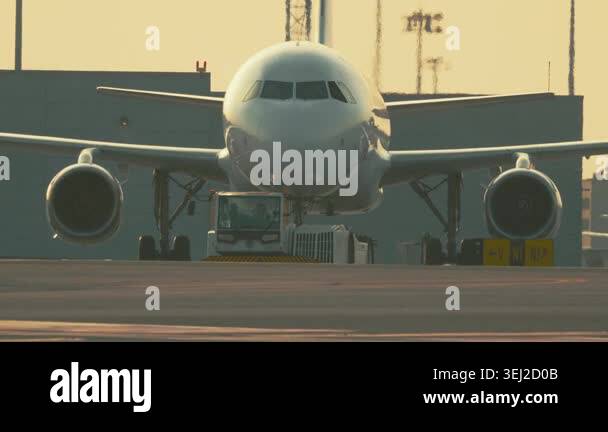 An airplane sits on the runway at the airport. The sun sets behind the ...