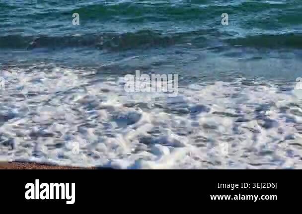Blue sea wave rolling onto coast with frothy white foam under sunlight ...