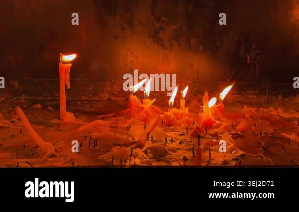 An orange church candle burns with bright flame among melted wax inside ...