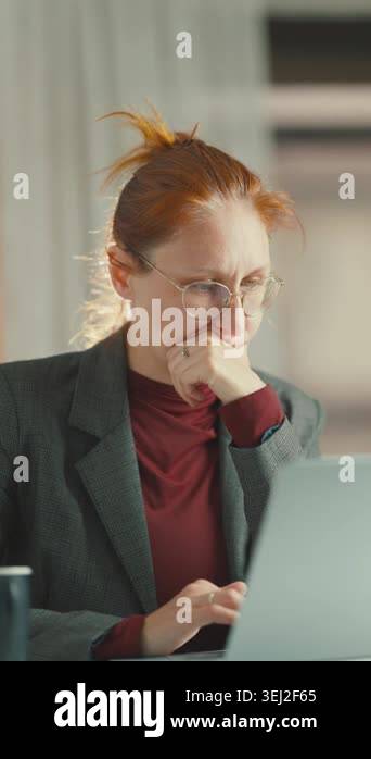 Thoughtful redhead businesswoman with glasses concentrating while ...