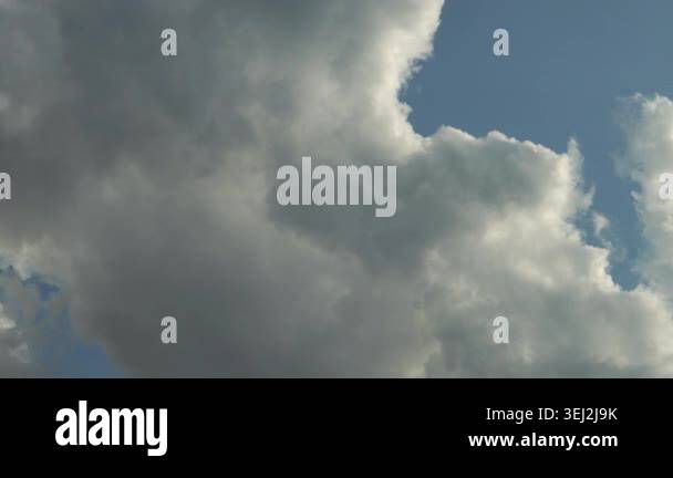 Large cumulus clouds float across a bright blue sky, creating a ...