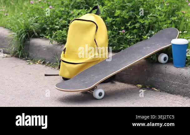 Yellow backpack, skateboard and coffee near the curb on a background of ...