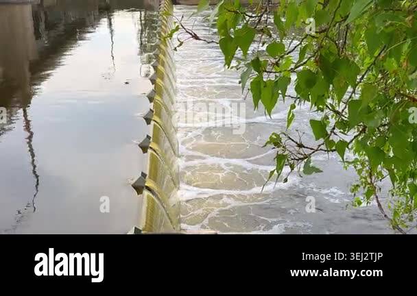 Water moves over a dam in Prague. The sunlight reflects on the waters ...