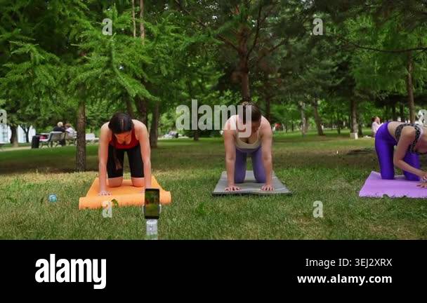 Women in sportswear demonstrating cat-cow pose on mats with children ...