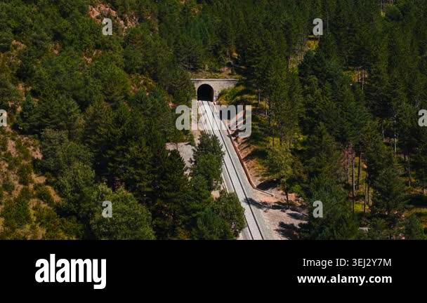 Train emerging from a dark tunnel onto a railway track surrounded by a ...