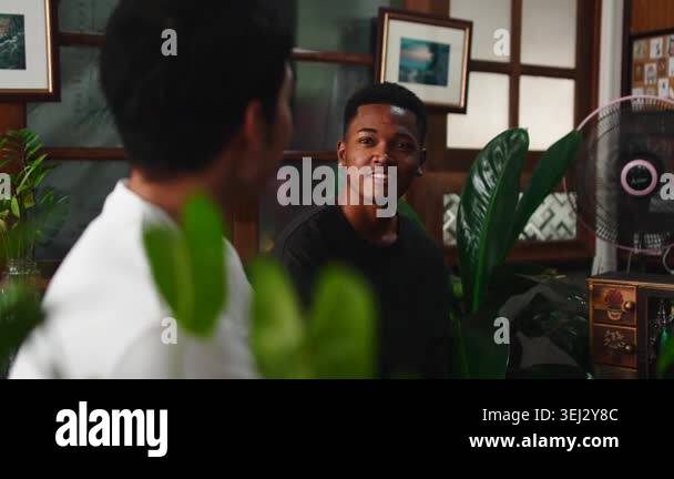 Two diverse young men, one asian and one black, talking and laughing ...