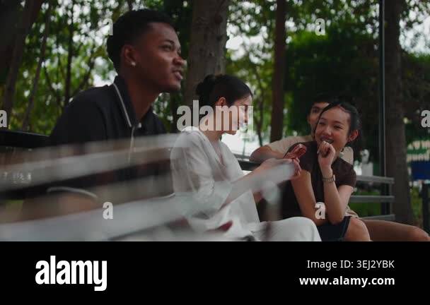 Group of young multiethnic friends sitting on a bench, having fun ...